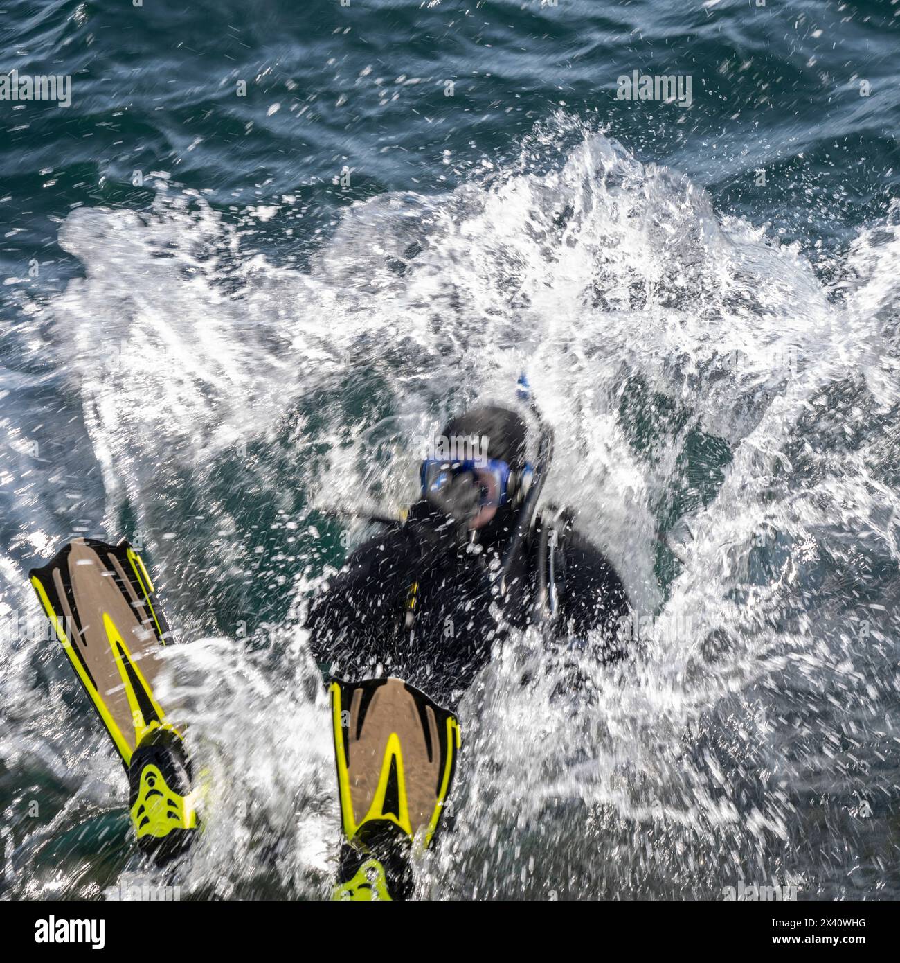 Diver in full diving gear plunges backwards into the water with a large ...