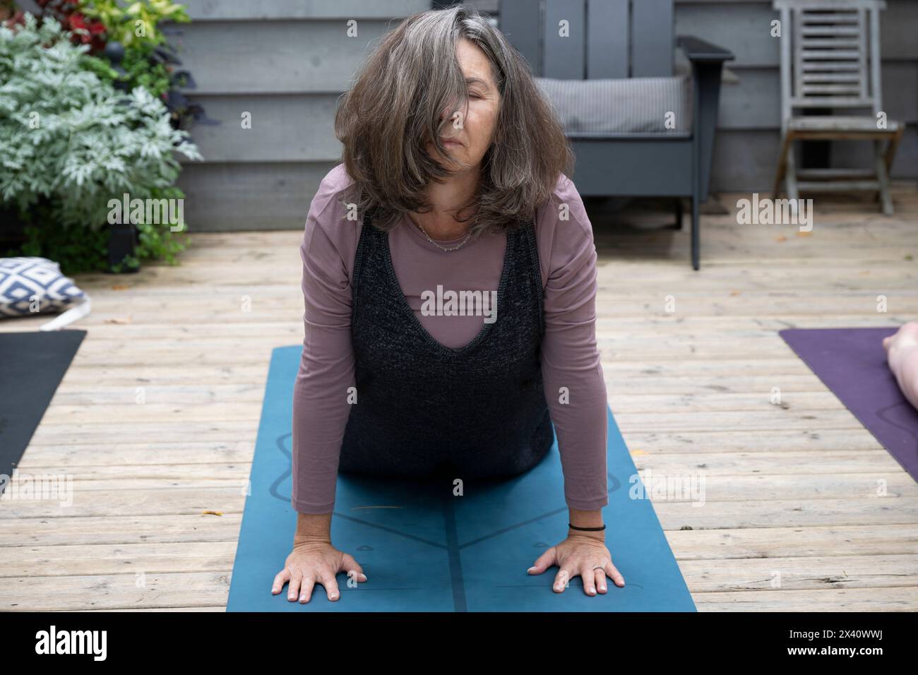 Senior woman doing yoga on a wooden deck, in a cobra pose (Bhujangasana ...