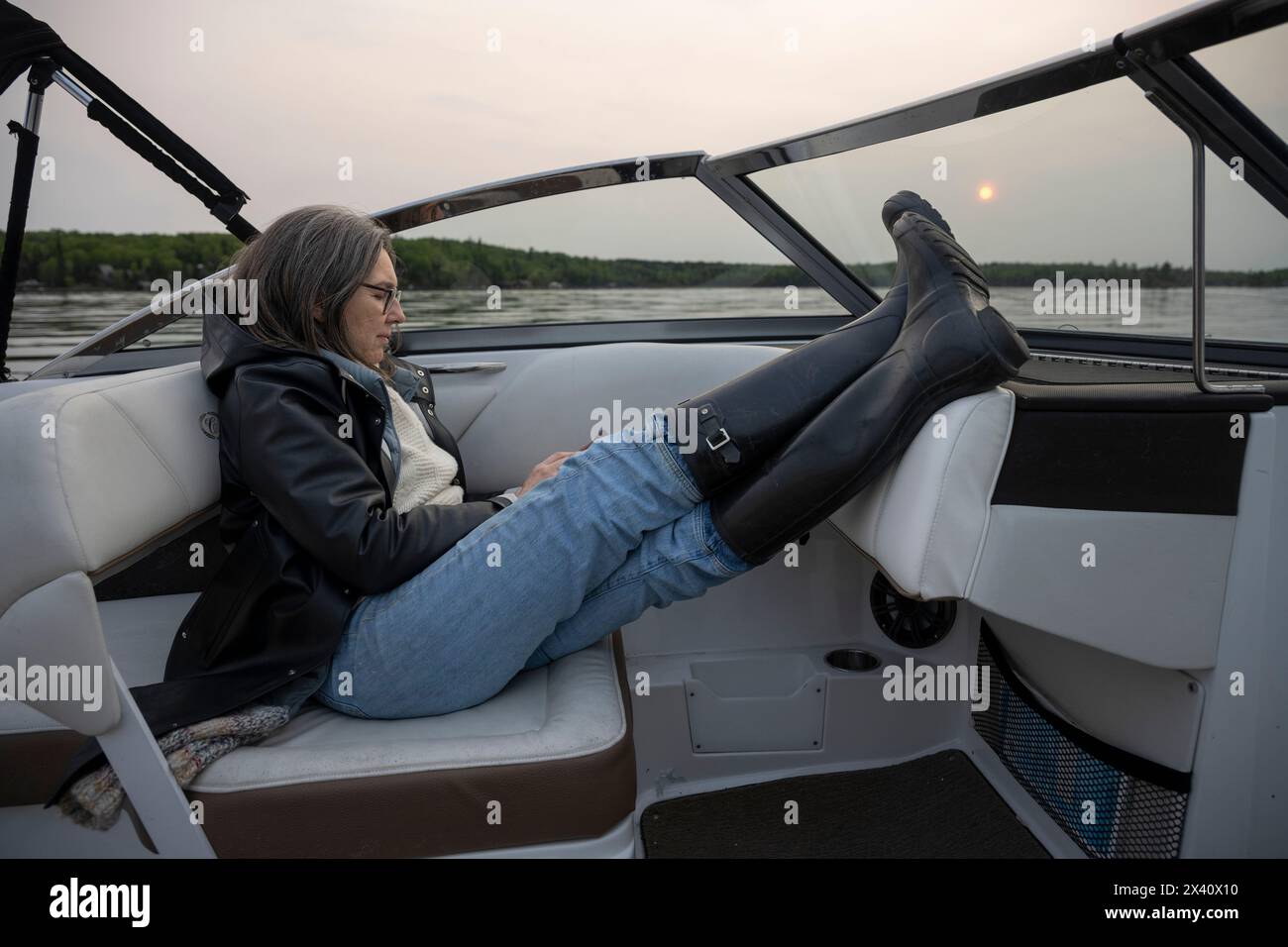Woman relaxes and uses her smart phone in a motorboat at sunset, with ...