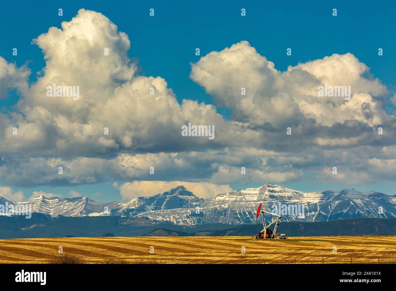 Pumpjack in a cut field with mountain range and dramatic clouds with ...