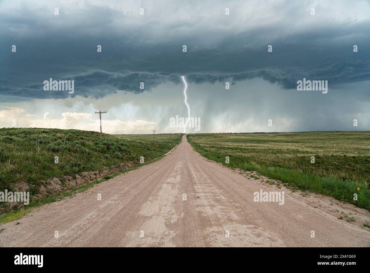 Lightning bolt strikes from a thunderstorm while a lonely road leads ...