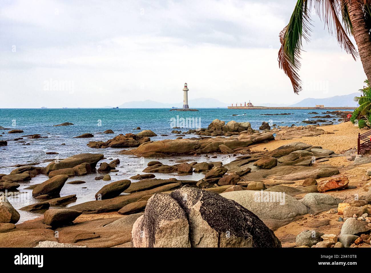 View of a lighthouse in the sea near a rocky shore with palm trees ...