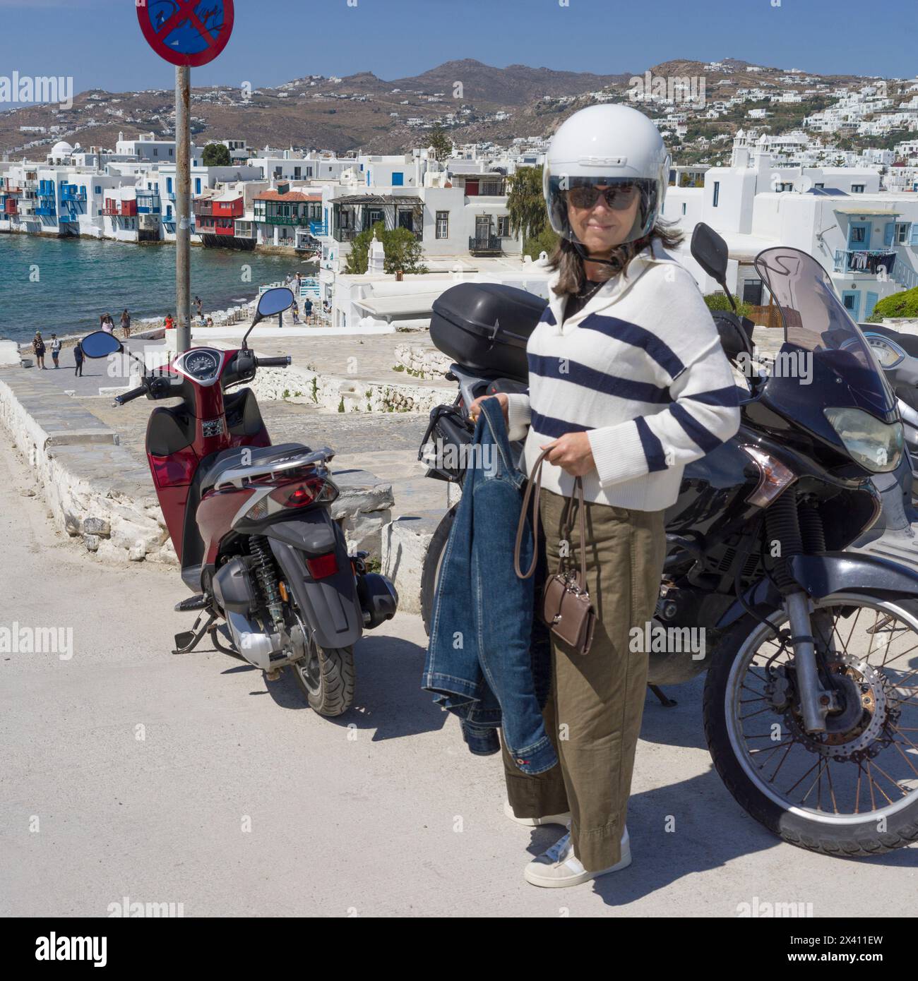 Woman in helmet standing with a motorcycle along the coast of Mykonos ...