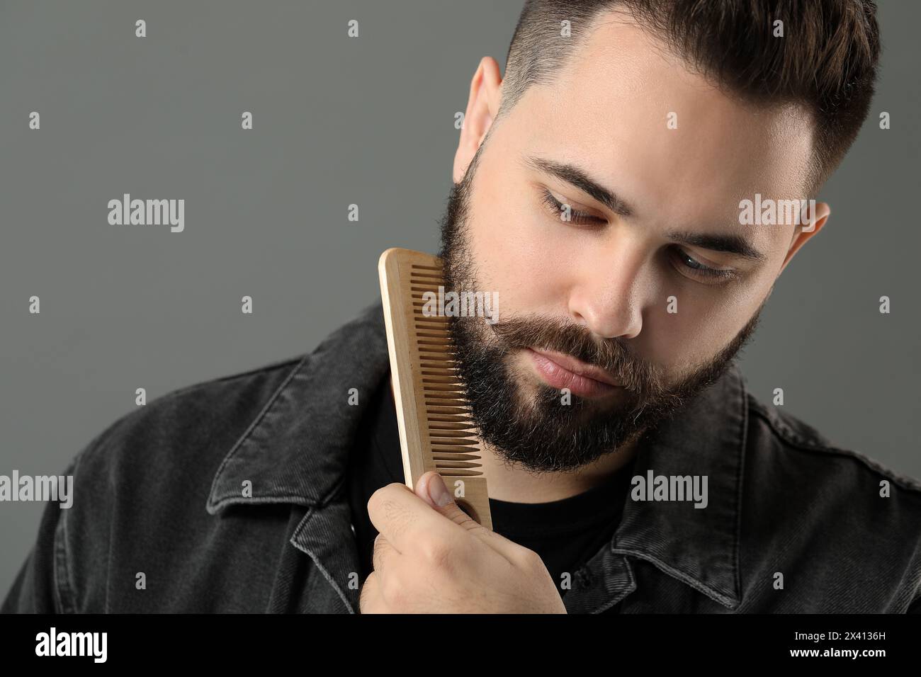 Handsome young man combing beard on grey background Stock Photo - Alamy