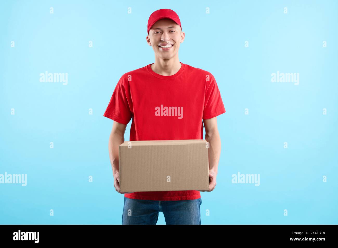 Happy courier with parcel on light blue background Stock Photo - Alamy