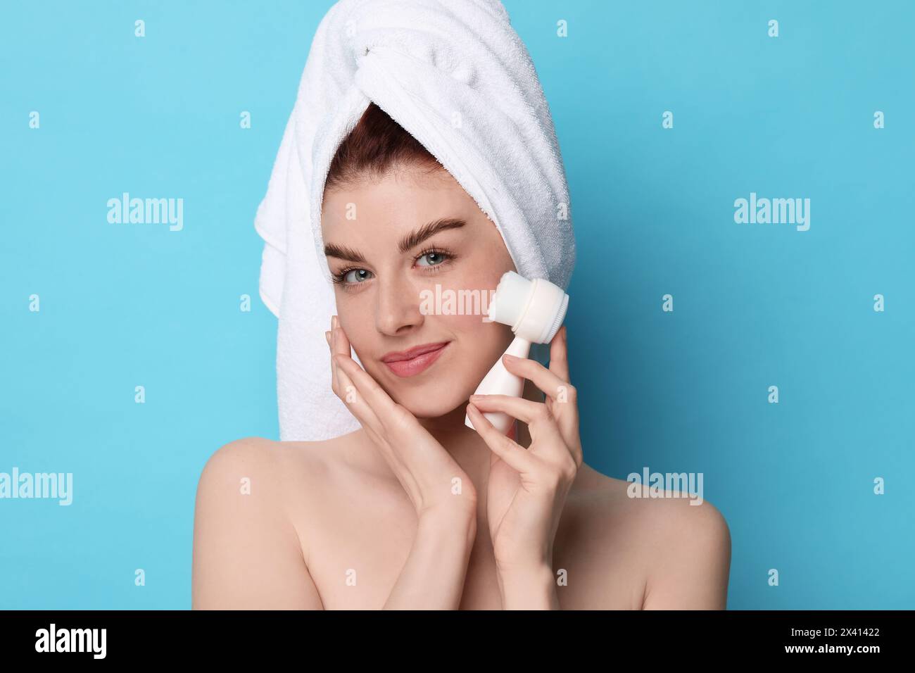 Washing face. Young woman with cleansing brush on light blue background ...