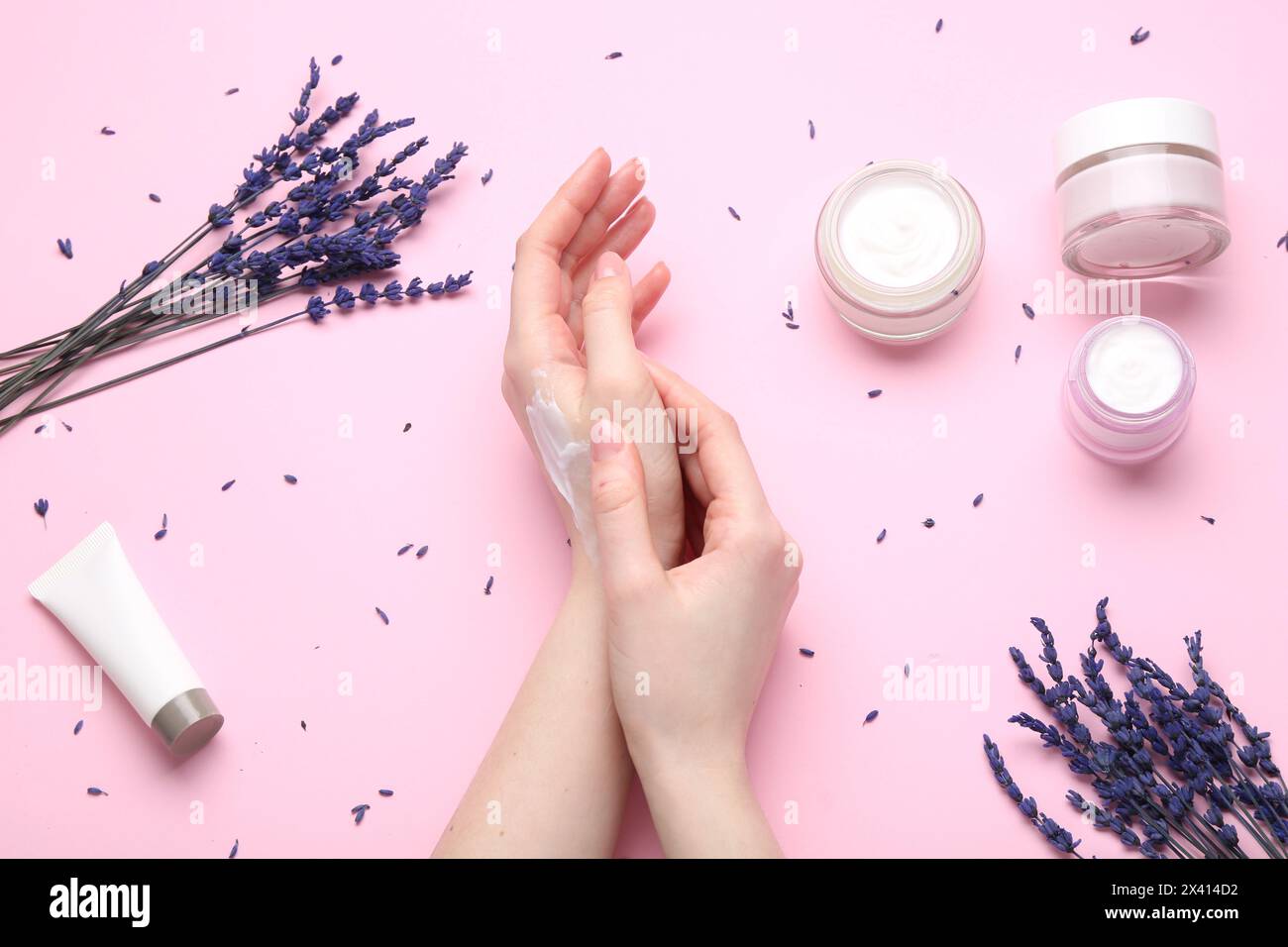 Woman applying hand cream and lavender flowers on pink background, top ...
