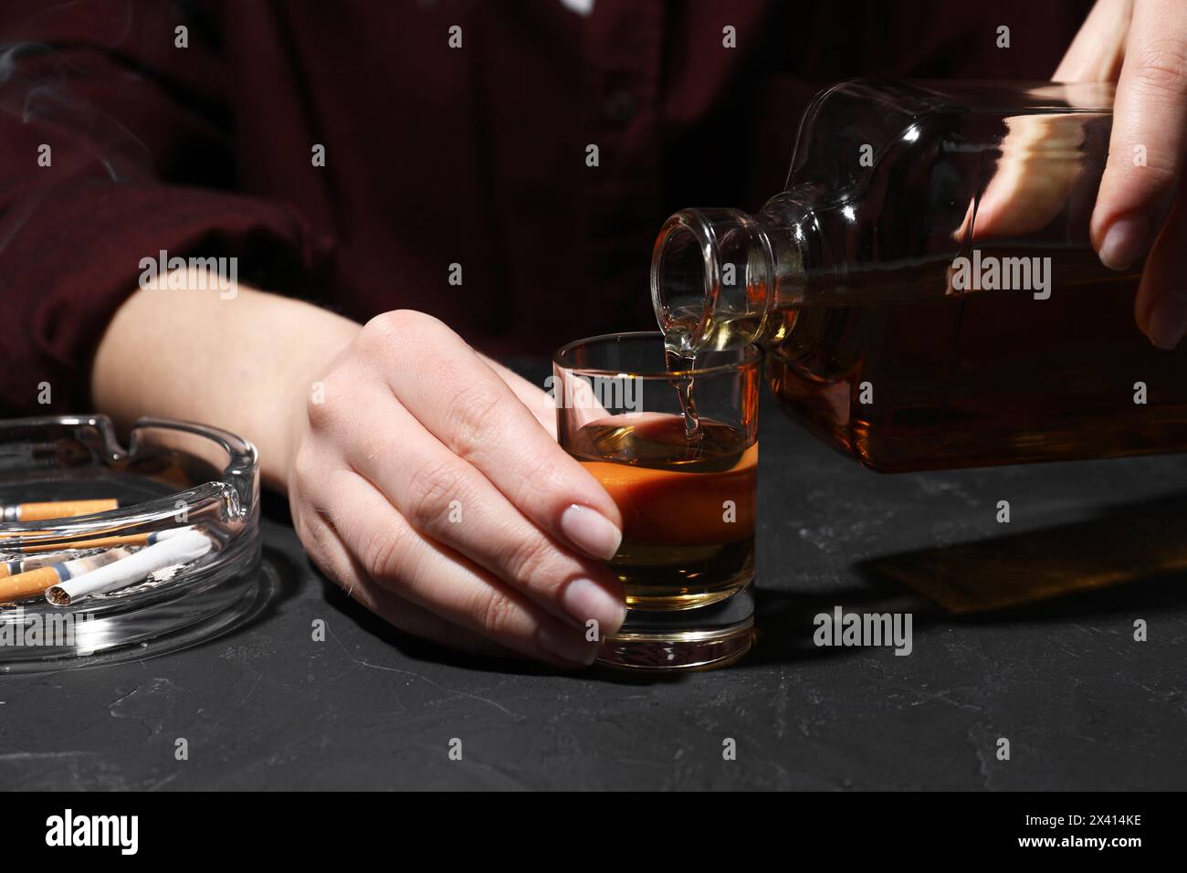 Alcohol addiction. Woman pouring whiskey from bottle into glass at dark ...