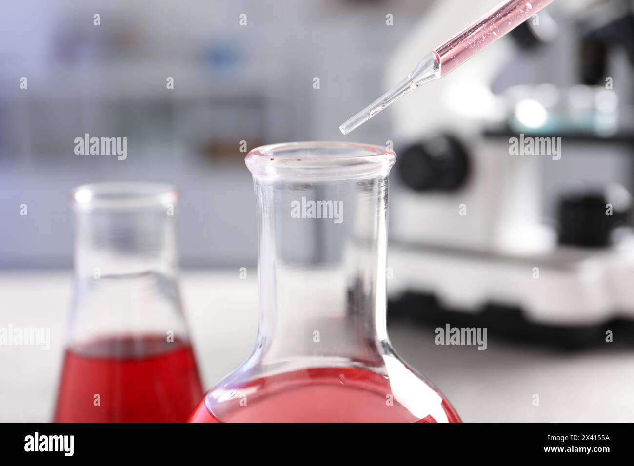 Laboratory analysis. Dripping red liquid into flask at light grey table ...