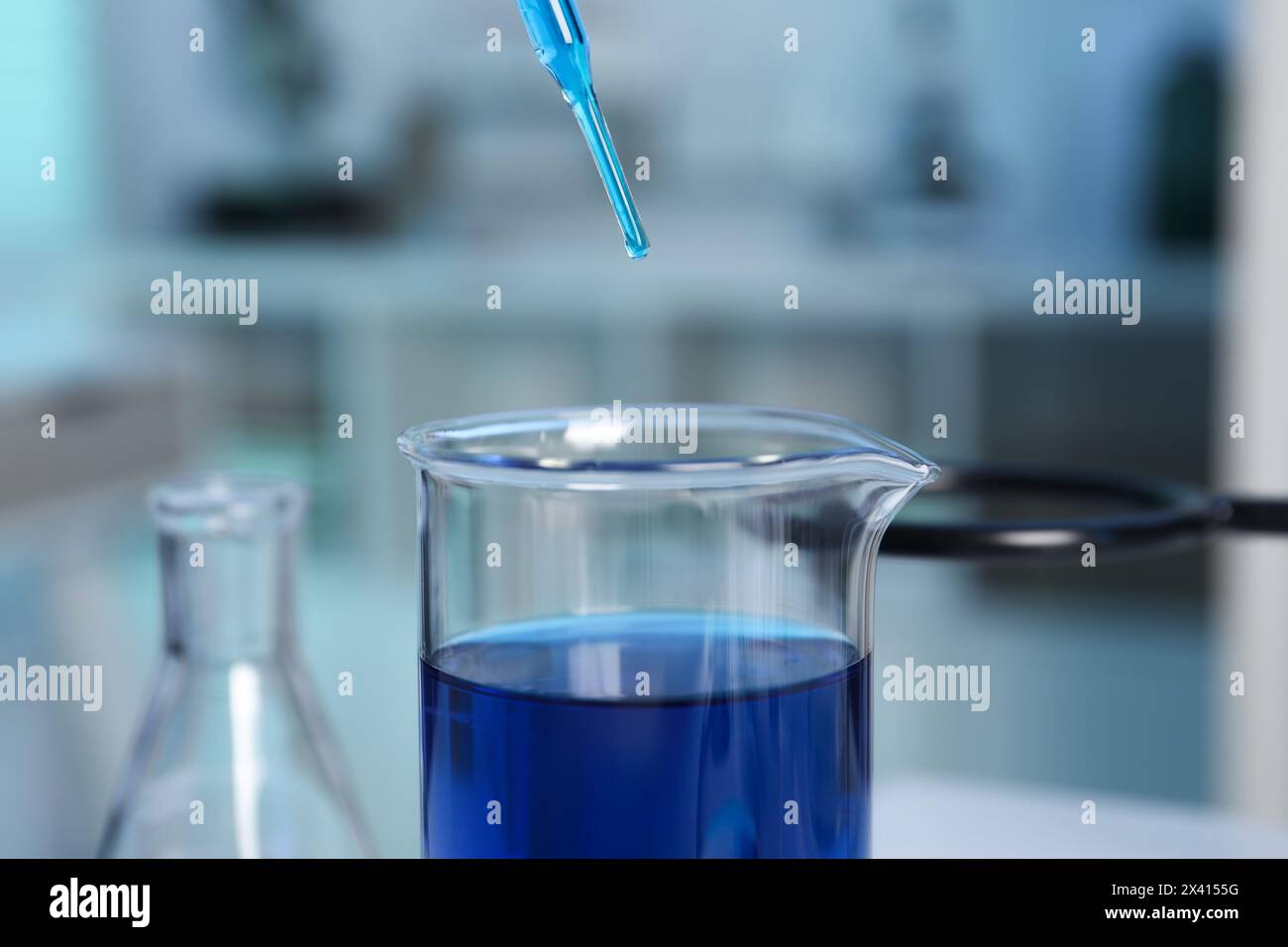 Laboratory analysis. Dripping blue liquid into beaker on table, closeup ...