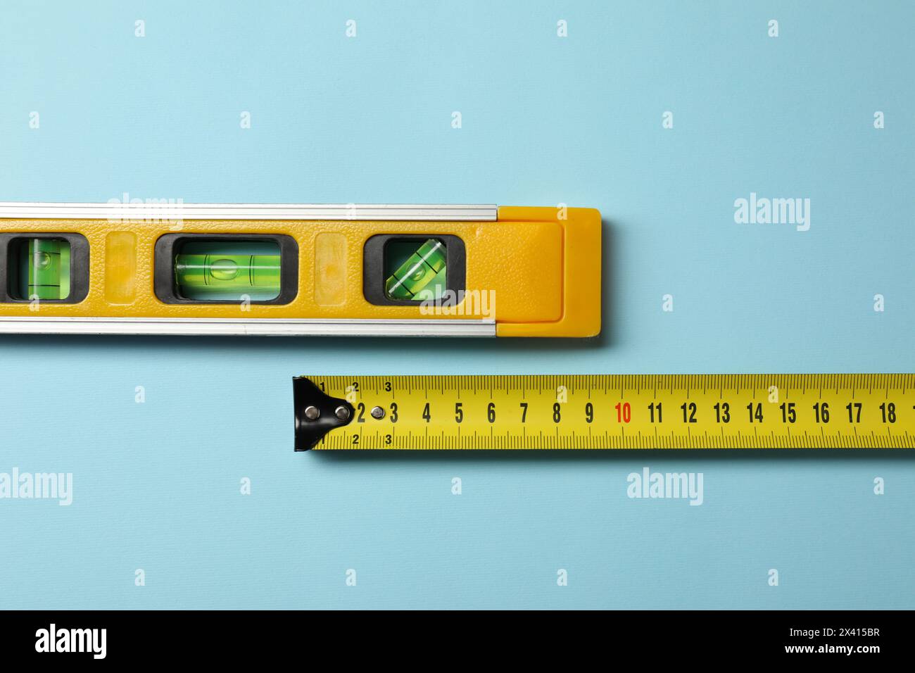 Building level and tape measure on light blue background, top view ...