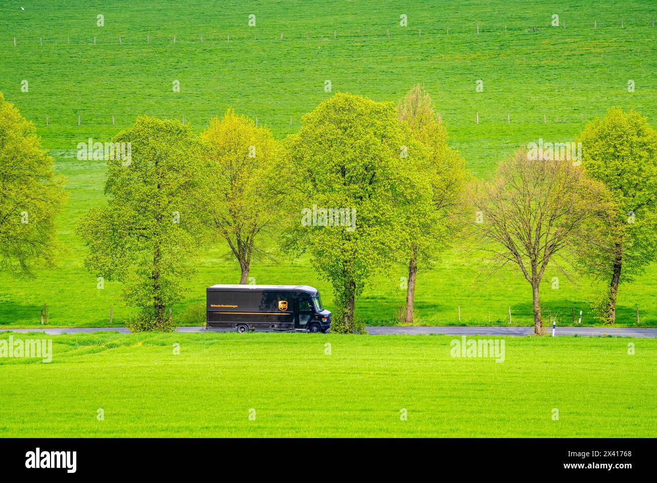 UPS delivery van on a country road, green fields, meadows, trees line ...