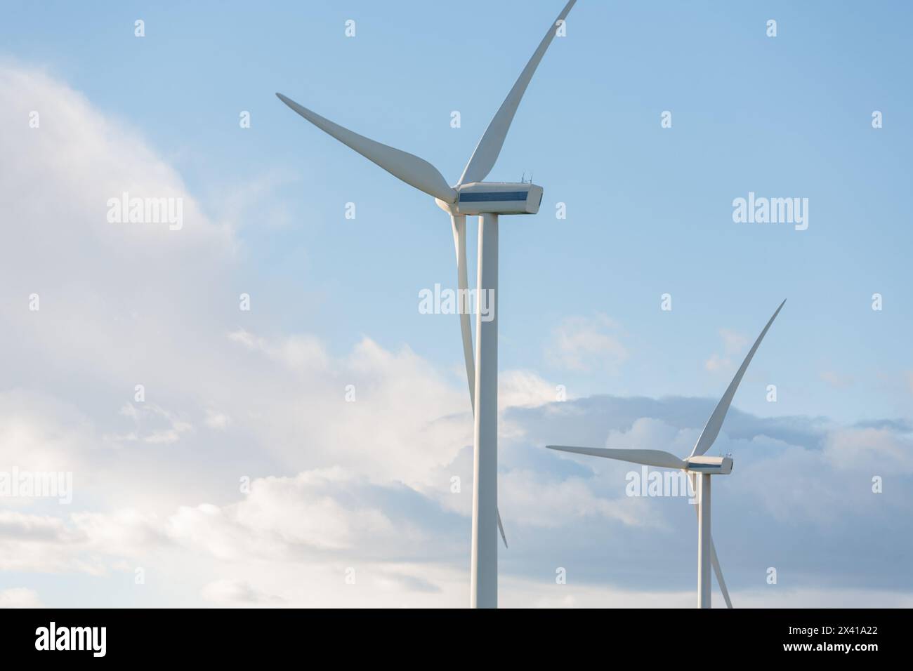 Two wind turbines are standing tall in the sky, with one of them being ...