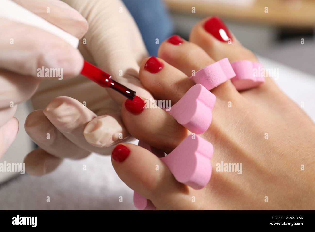 Pedicurist painting client`s toenails with red polish in beauty salon ...