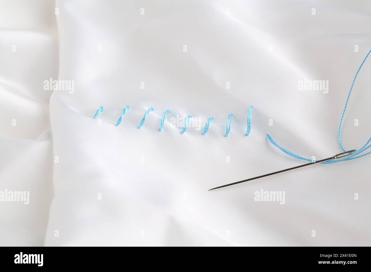 Sewing needle with thread and stitches on white cloth, top view Stock ...