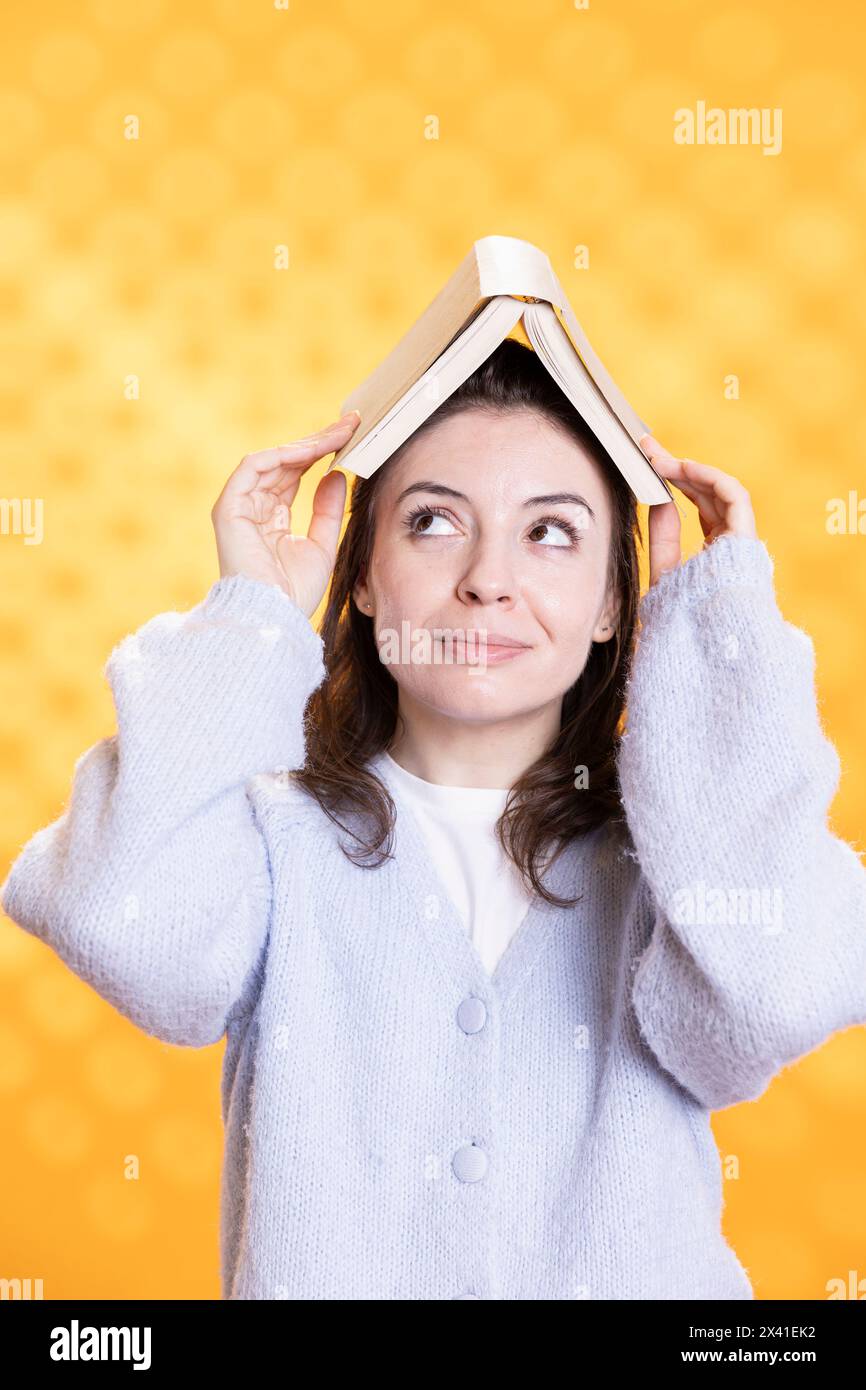 Portrait of joyous woman placing book on head, acting zany, enjoying ...