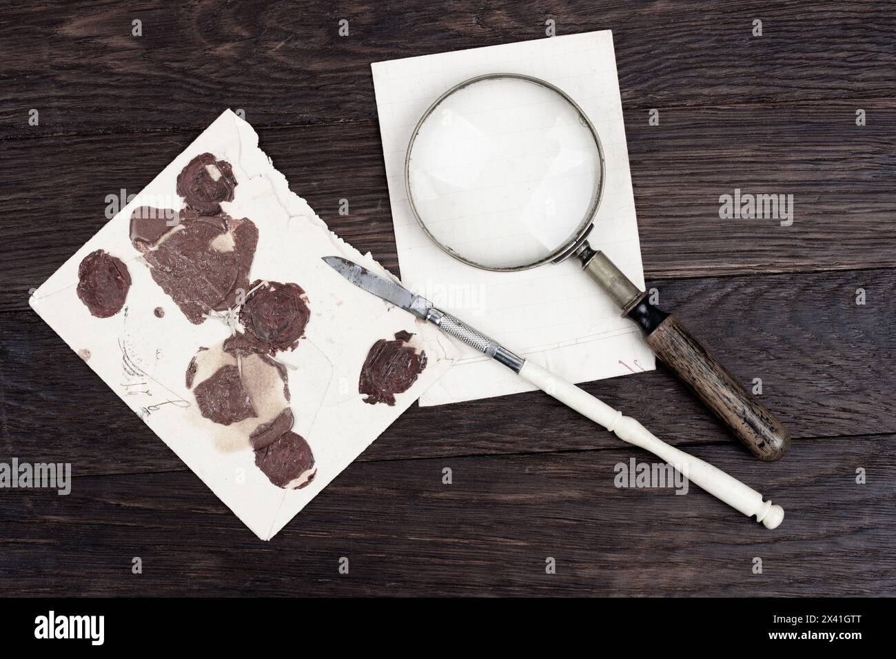 Retro envelope opener knife with magnifying glass and vintage letter envelope on wooden desk ...