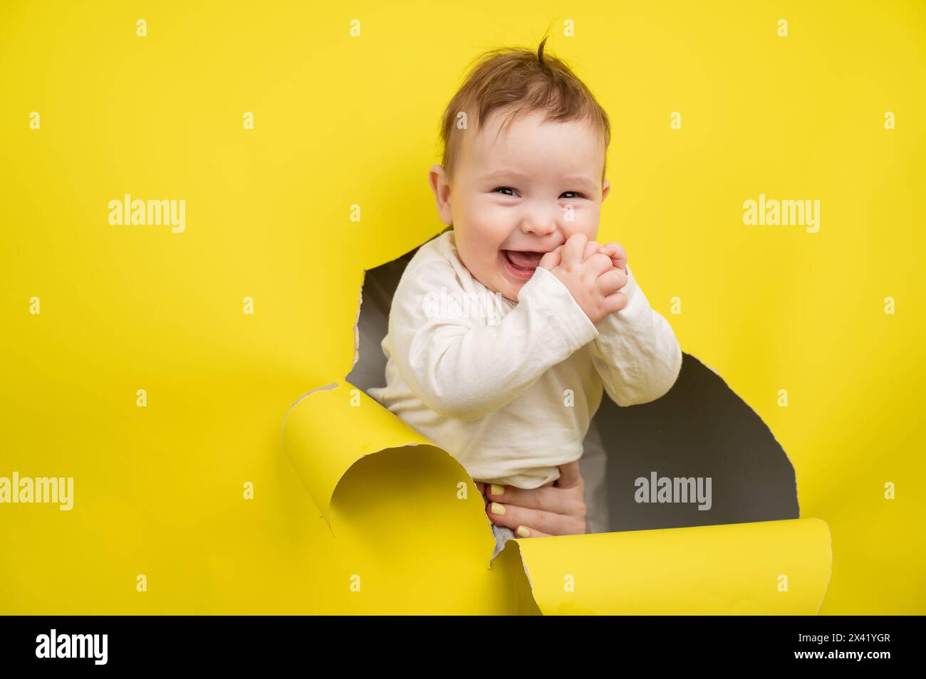Cheerful baby rips and sticks out through yellow cardboard background ...