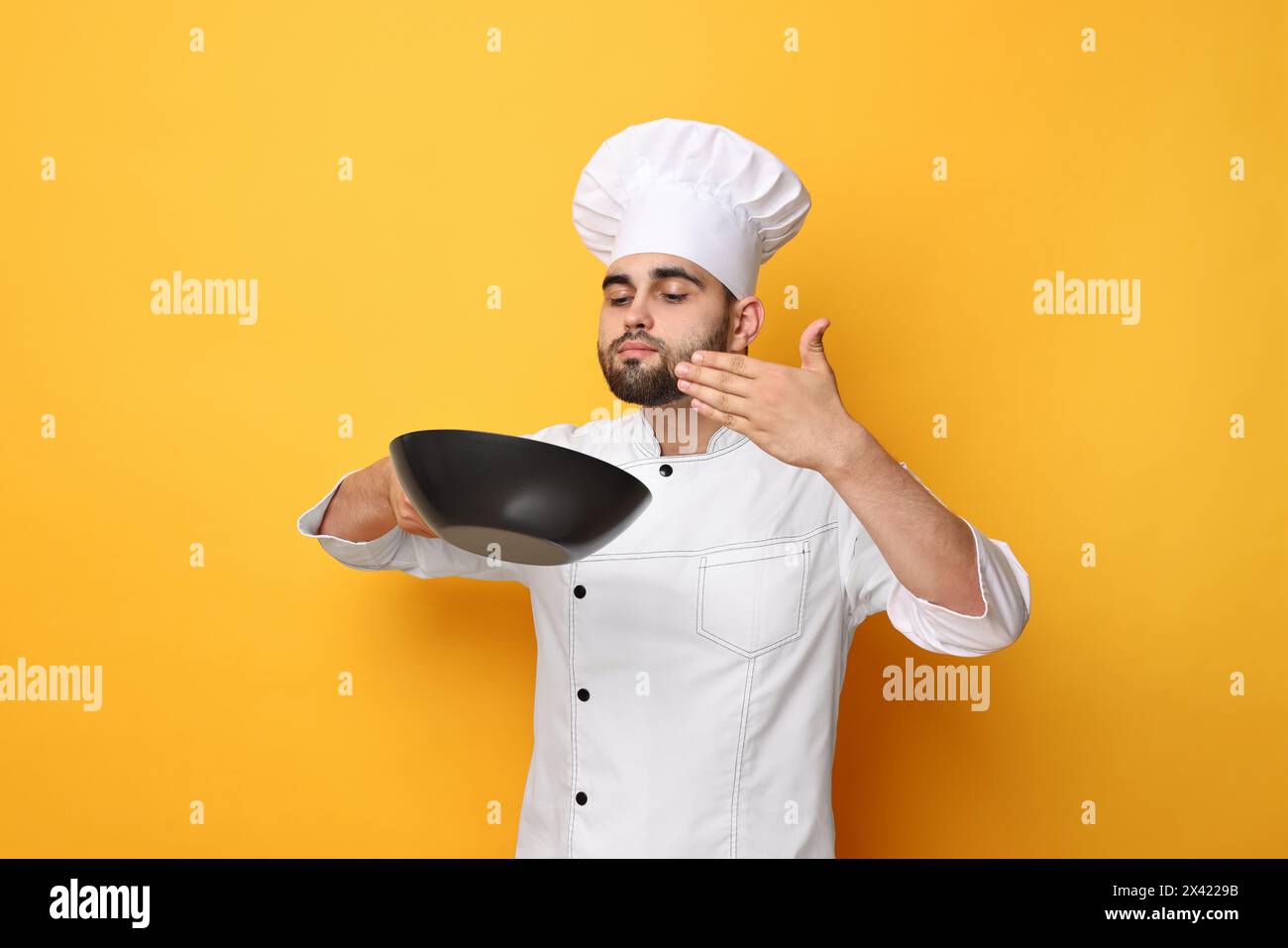 Professional chef smelling something in wok on yellow background Stock ...