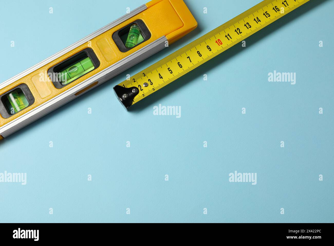 Building level and tape measure on light blue background, top view ...