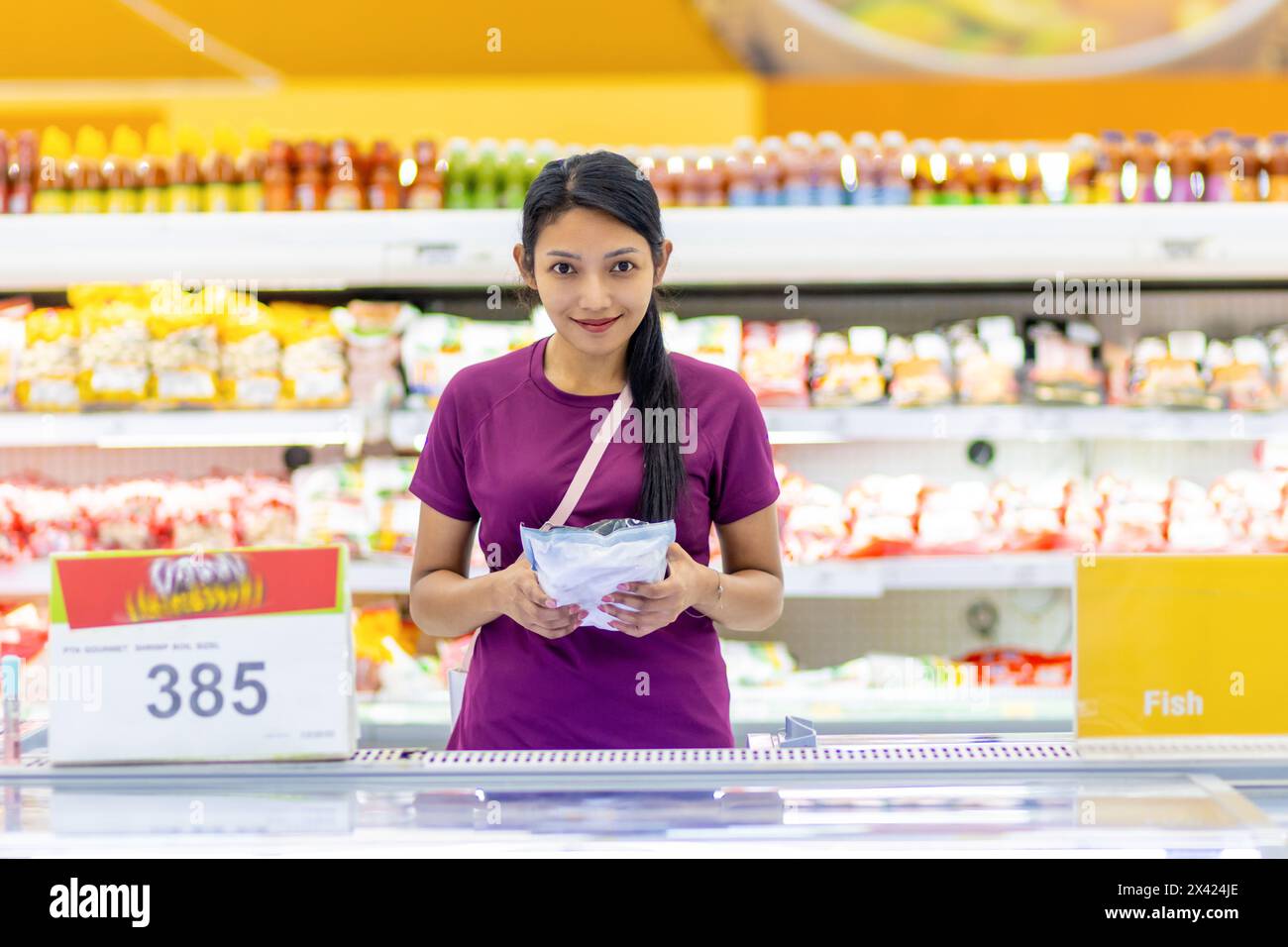 A young woman stands with a package of frozen food at the freezer counter in the store Stock ...