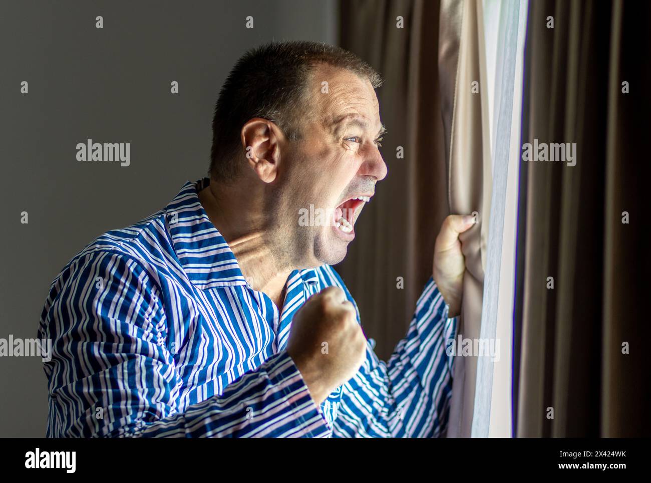 Aggressive man in striped pajamas looks out the window and scream Stock ...