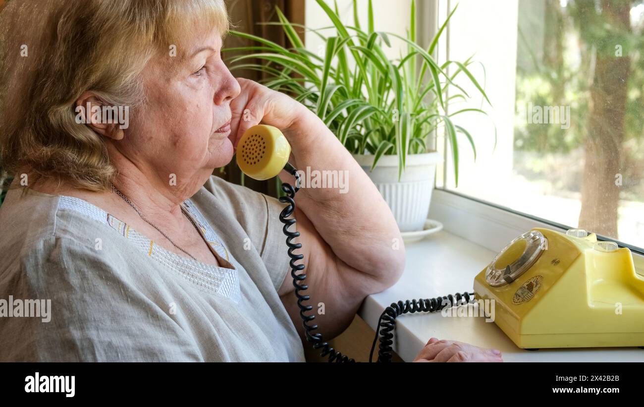Old woman receives phone call. Grandmother talking on an old disc phone ...