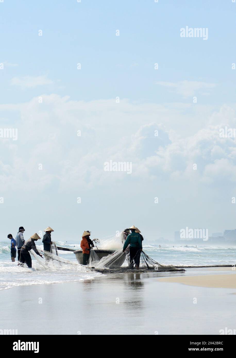 Vietnamese fishermen pulling out a large fishing net from the beach in ...