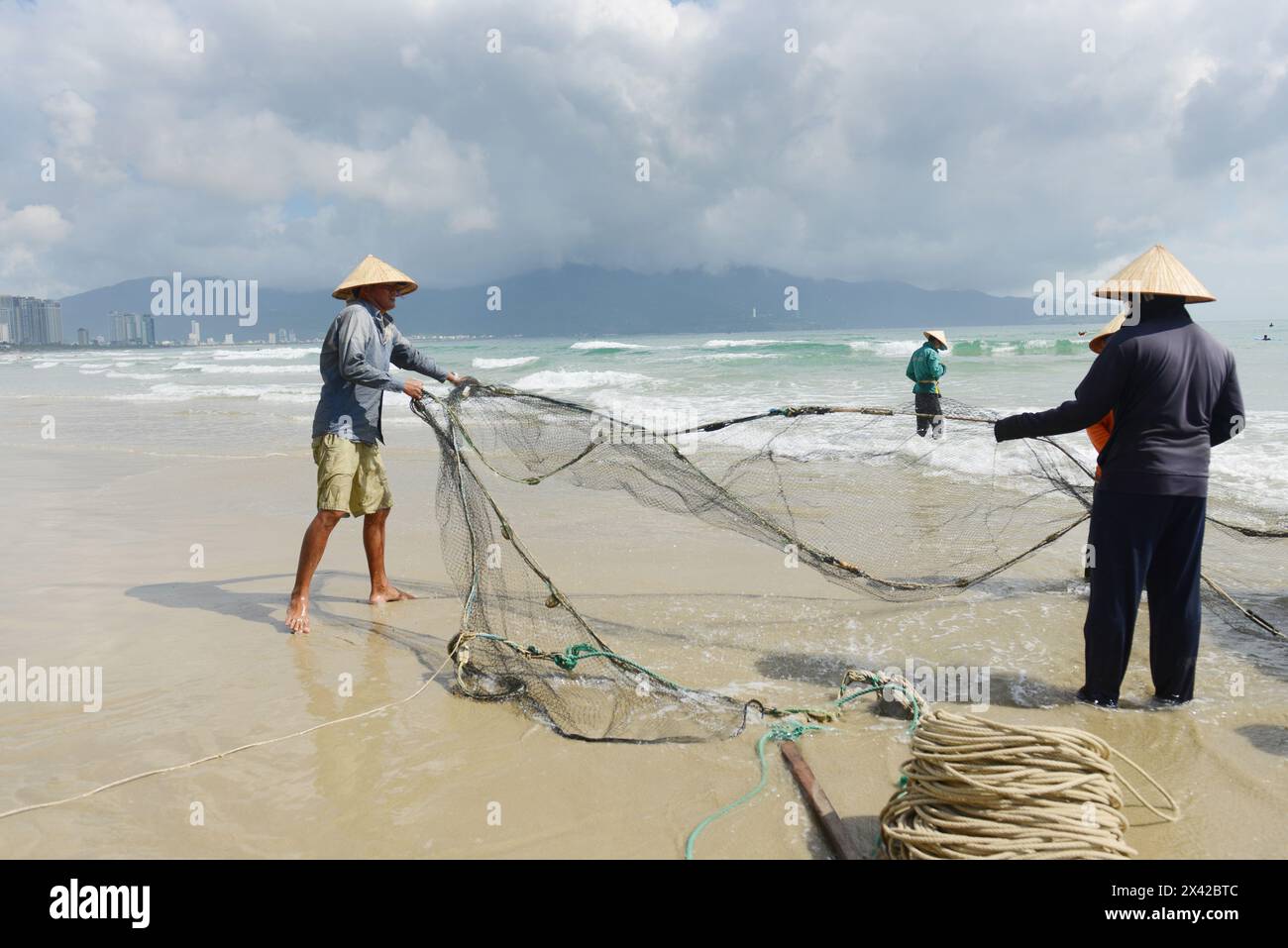 Vietnamese fishermen pulling out a large fishing net from the beach in ...