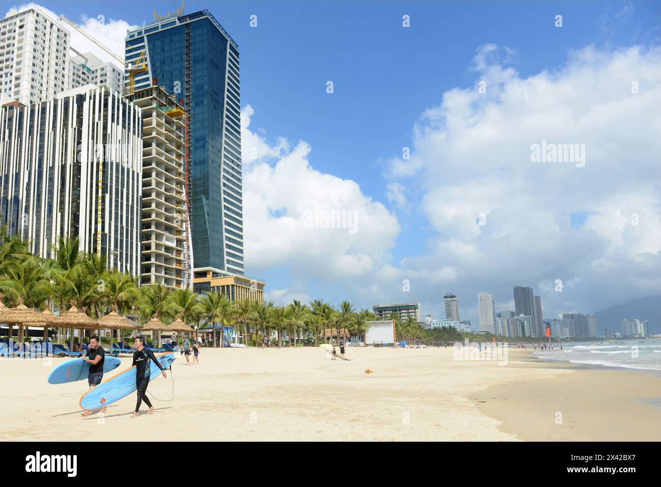 Surfers walking on the beautiful long white sand beach along the ...