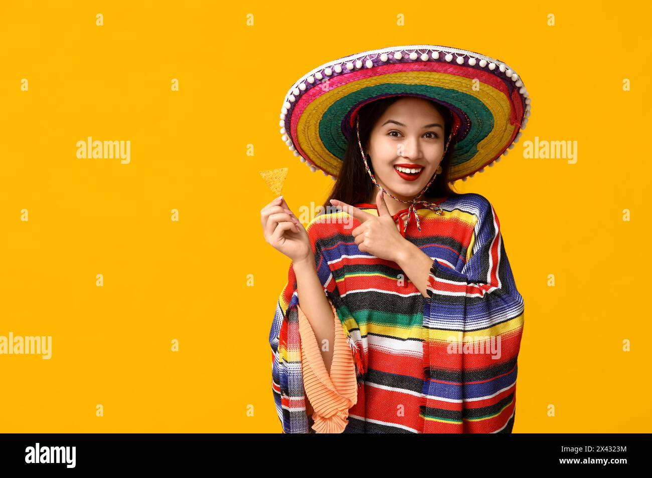 Portrait of young woman in colorful poncho and sombrero pointing at ...