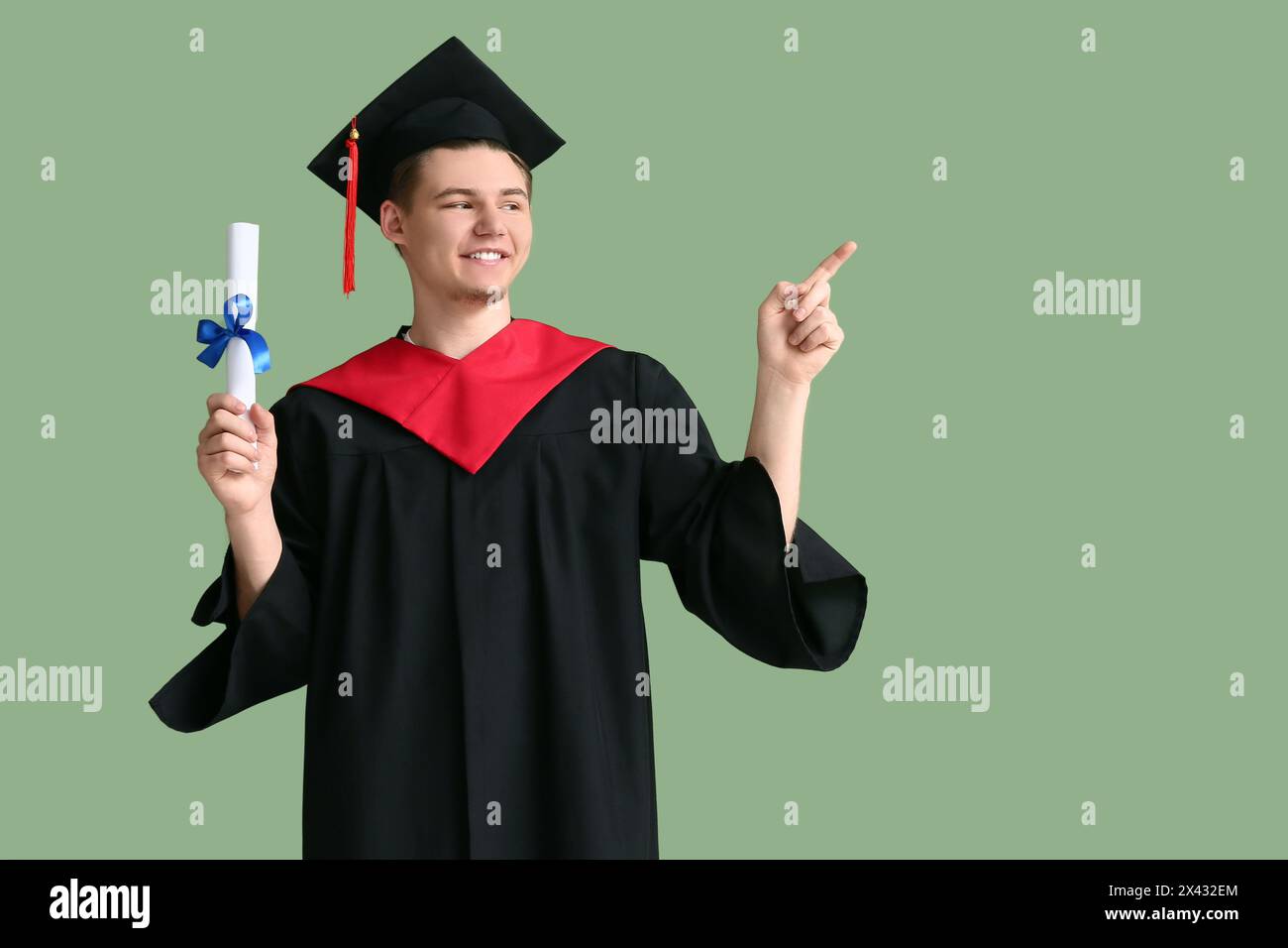 Happy male graduate with diploma pointing at something on green ...