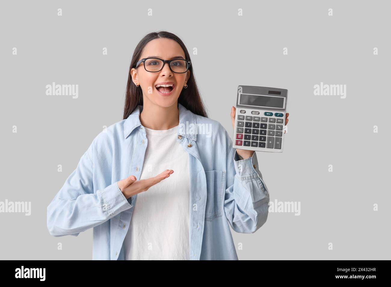 Happy young woman pointing at calculator on grey background Stock Photo ...