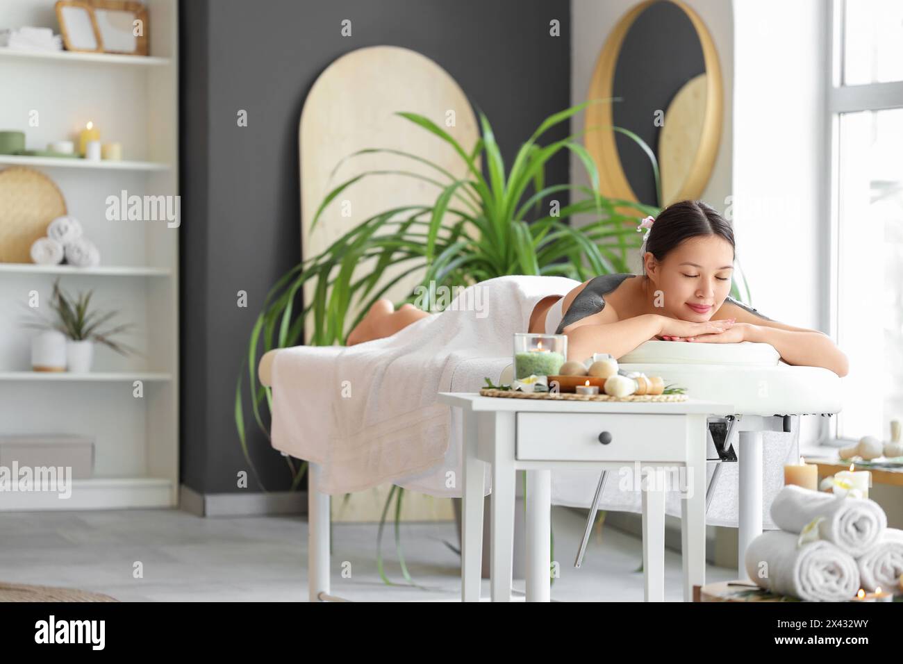 Beautiful Asian woman with mud on her shoulders lying in spa salon ...