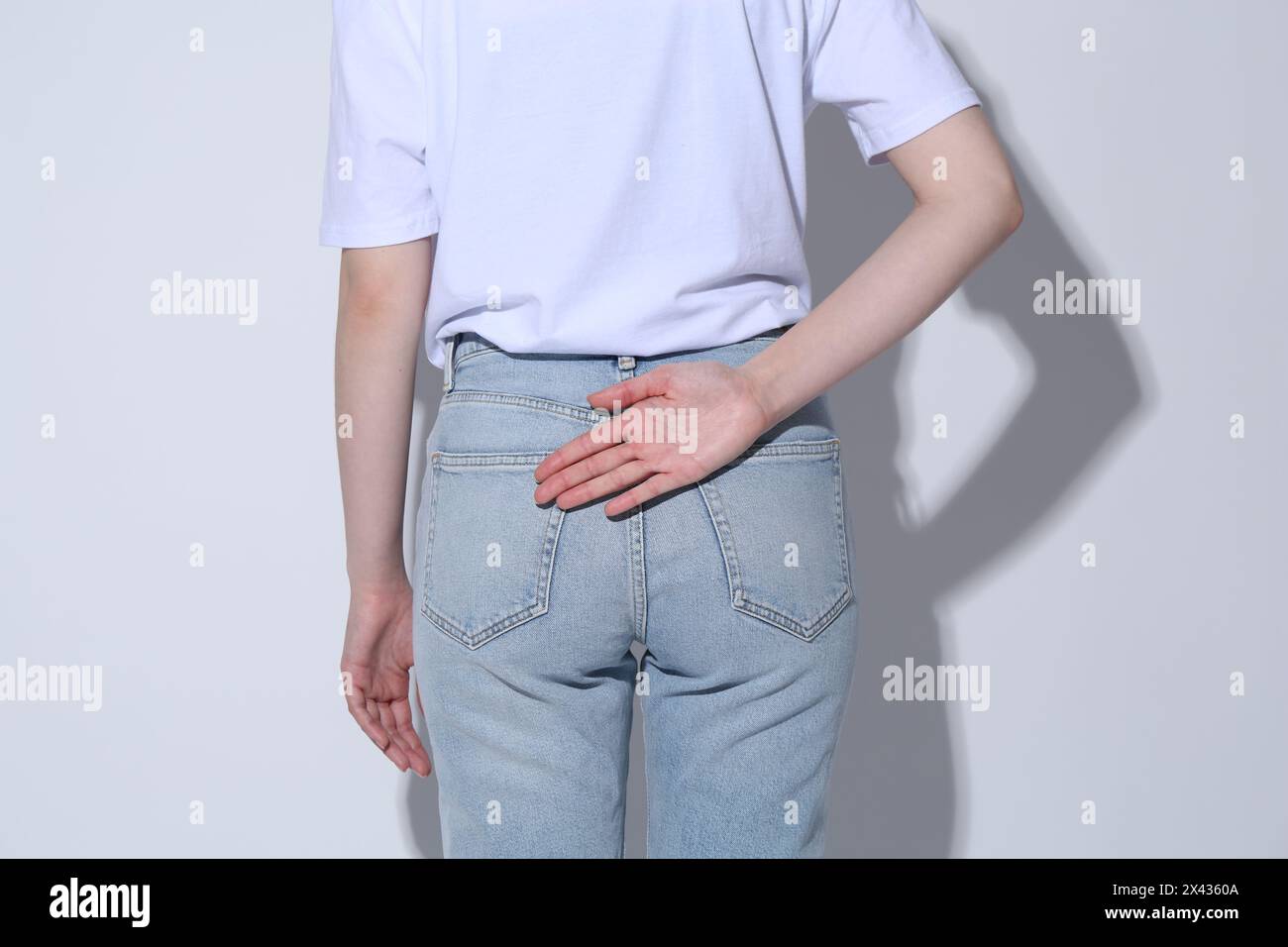 Woman showing open palm behind her back on light background, back view ...