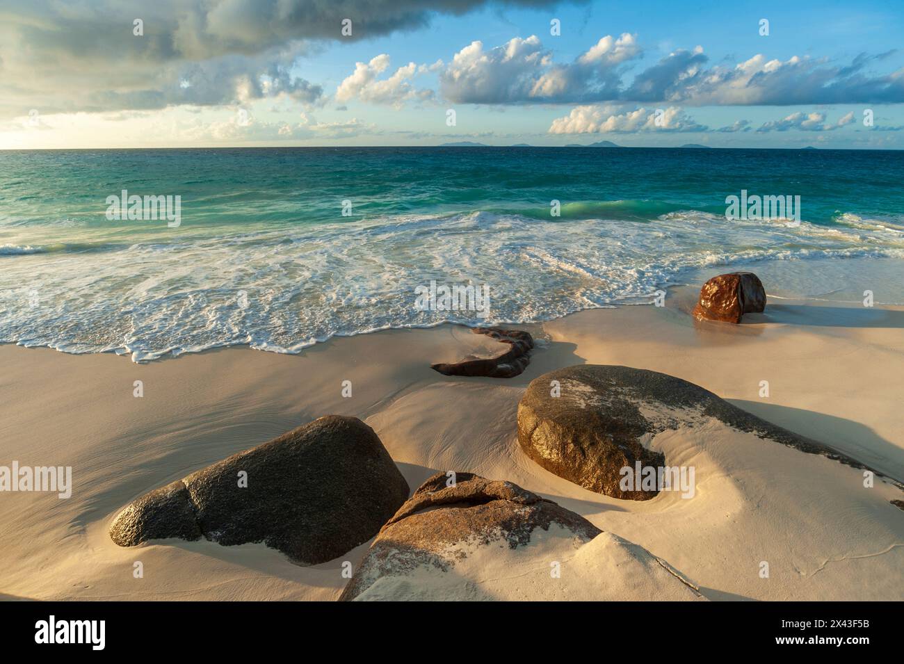 Surf surging towards boulders buried in sand on a tropical beach. Anse ...
