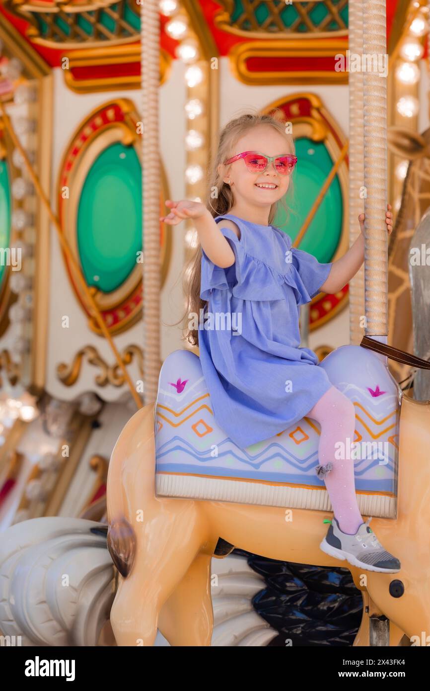 A happy little girl rides a carousel in the summer at an amusement park ...