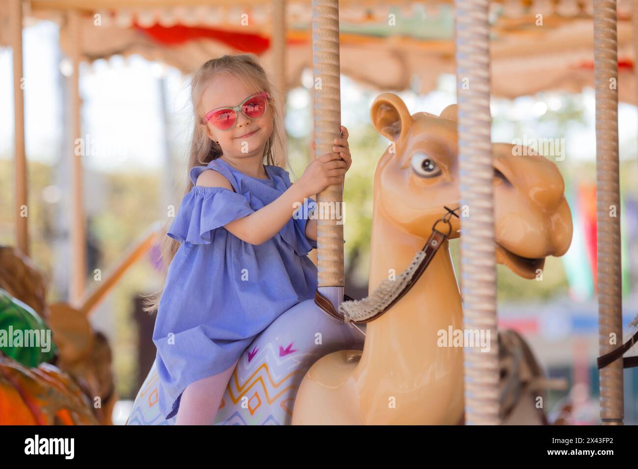 A happy little girl rides a carousel in the summer at an amusement park ...