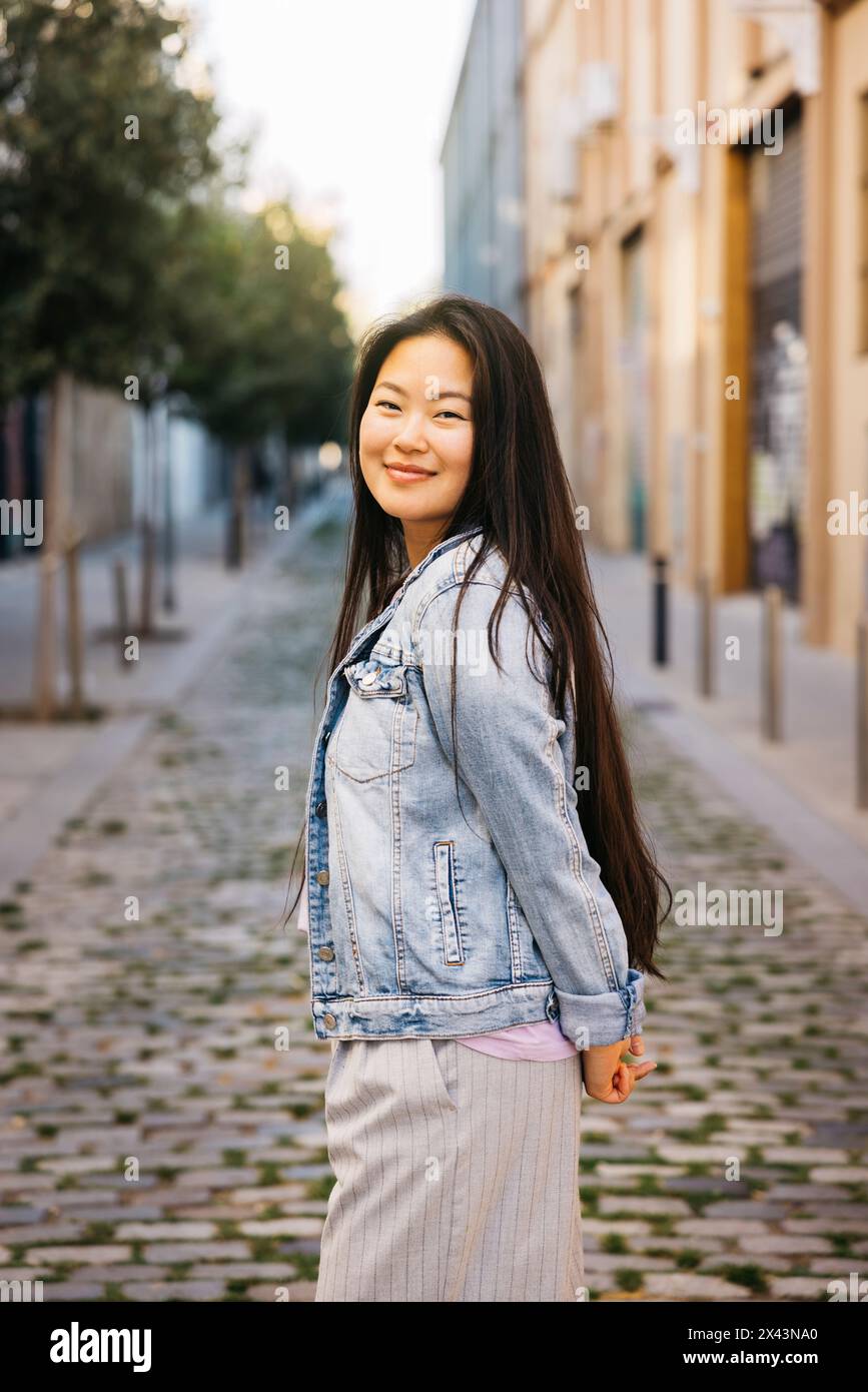 Portrait of a young beautiful smiling asian woman standing on sidewalk ...