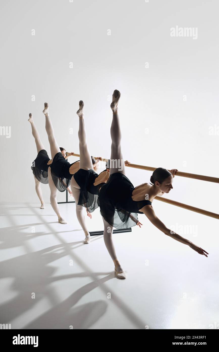 Four ballet dancers line up at barre, performing identical pose with ...