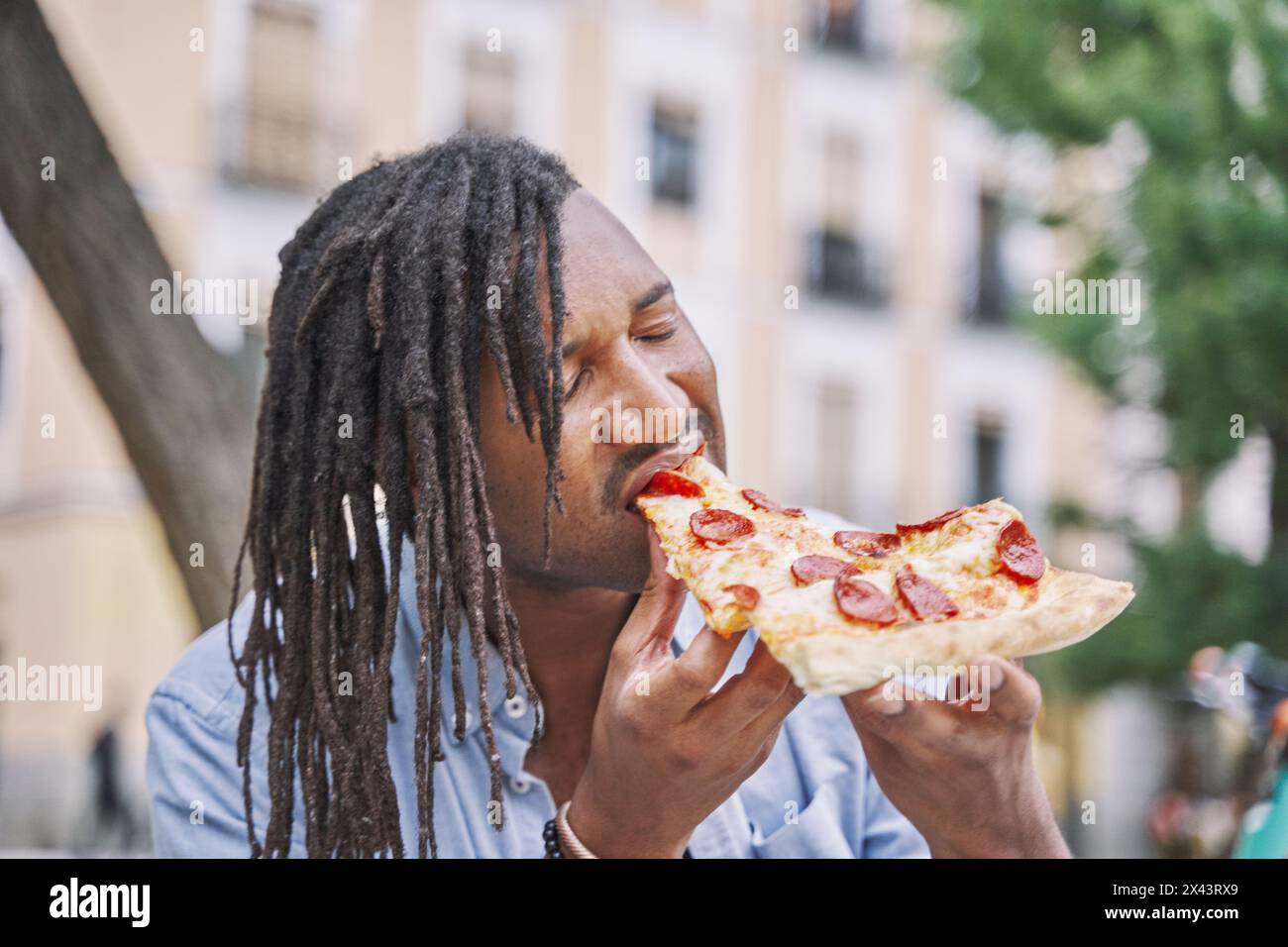 Young african man eating pizza slice outdoors. Man putting the whole ...