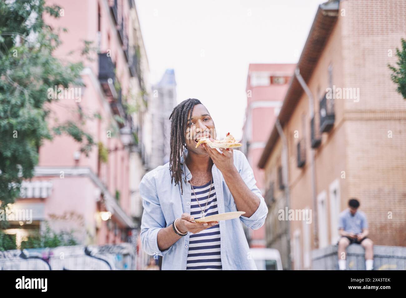 take-away food. man with braids eating a slice of pizza on the street ...