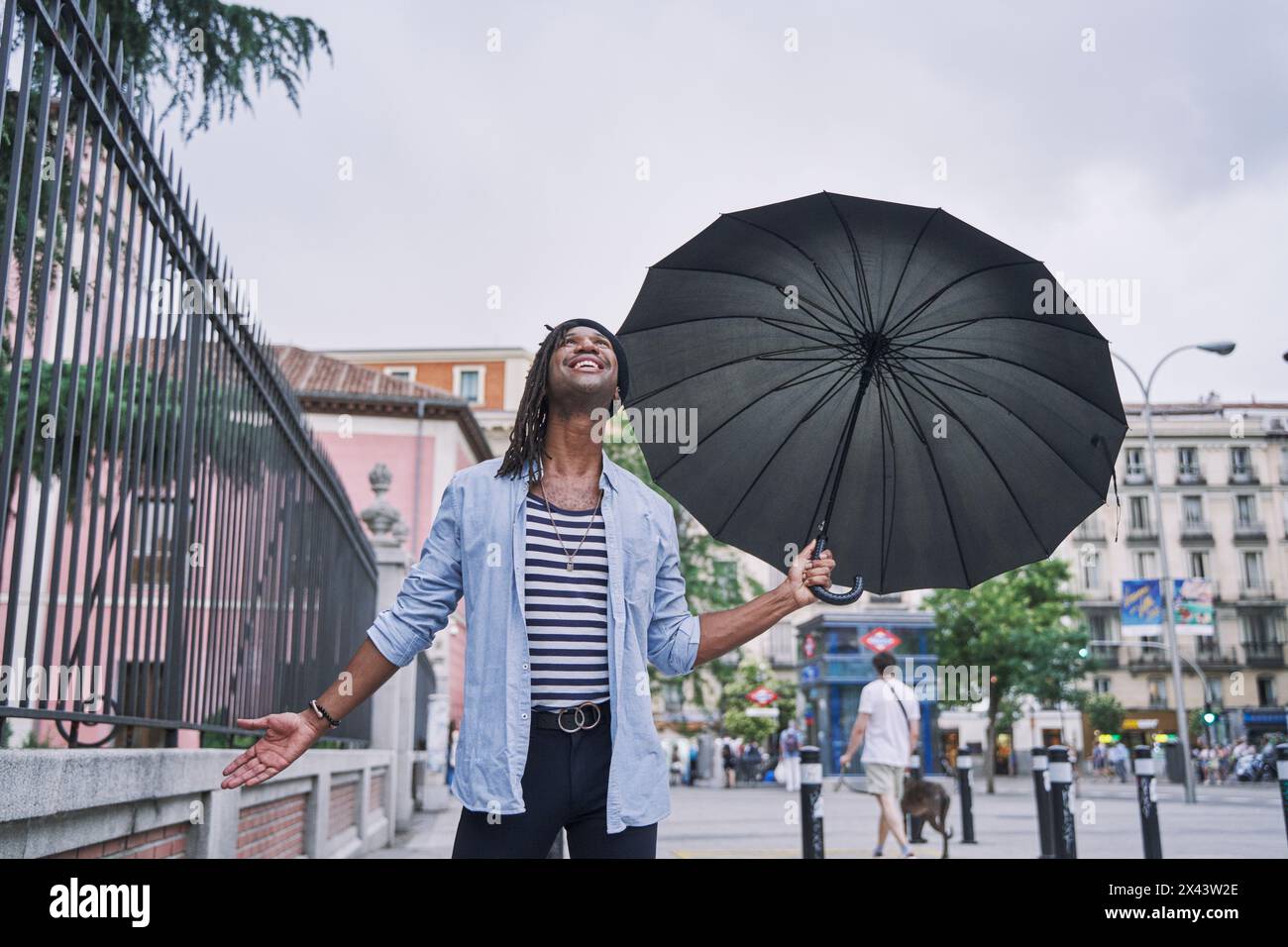 Attractive young man in the rain, holding his umbrella, looking up to ...