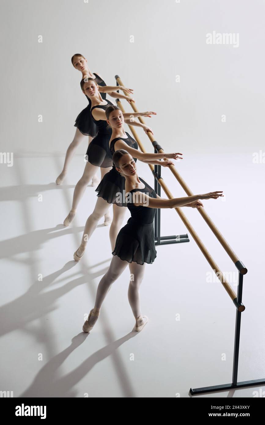 Four teens girls, ballet dancers practicing at barre, extending arm in ...