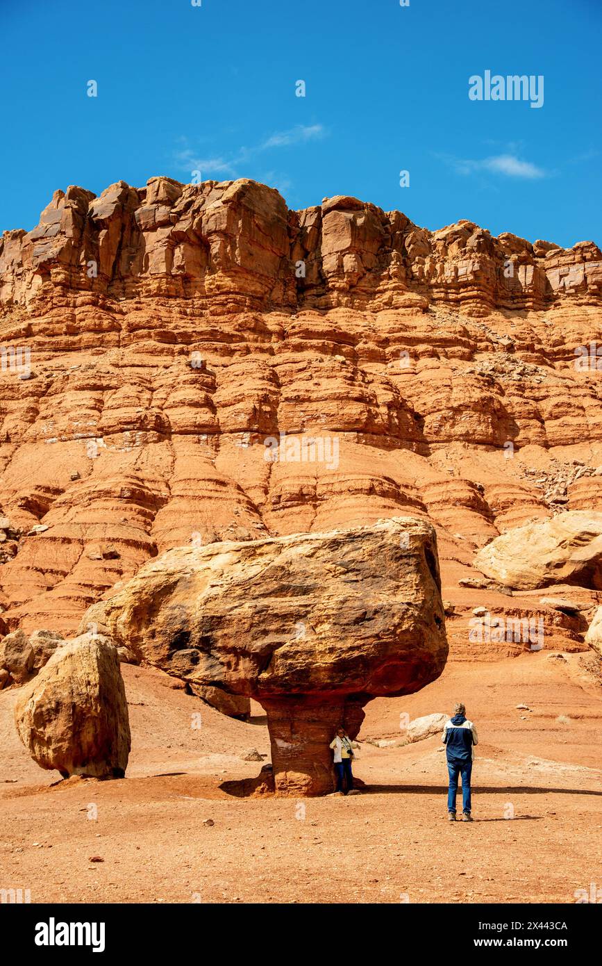 A woman stands below a large sandstone boulder as a man photographs her ...