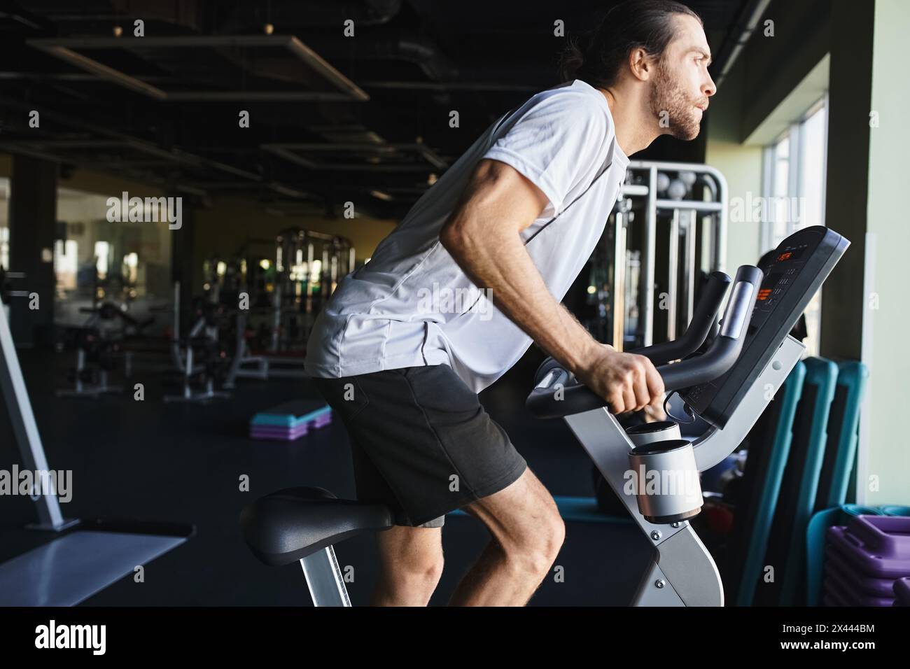 Muscular man vigorously cycling on a stationary bike in a gym ...