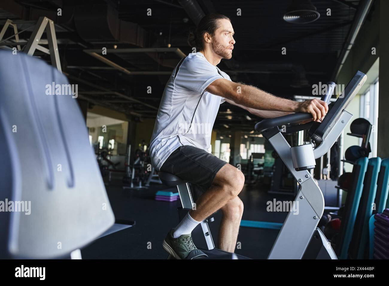 A muscular man is energetically cycling on a stationary bike at the gym ...