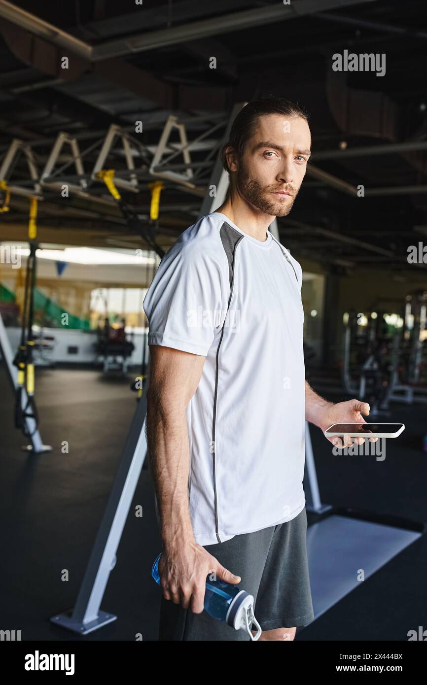 A muscular man hydrating with a water bottle in a gym while working out ...