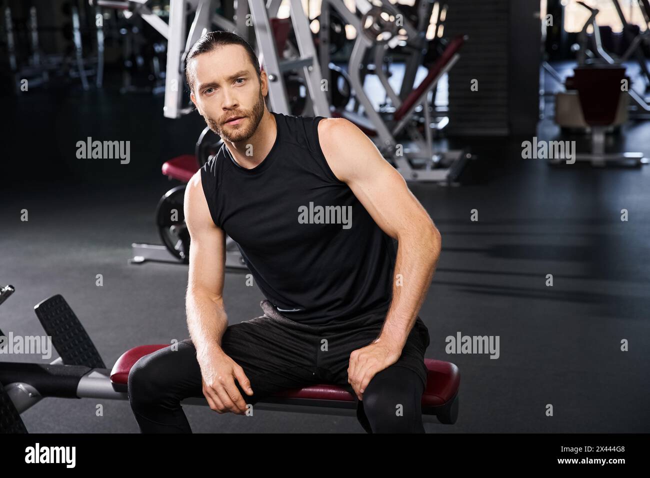 A focused man in athletic wear sits on a gym bench, deep in thought ...