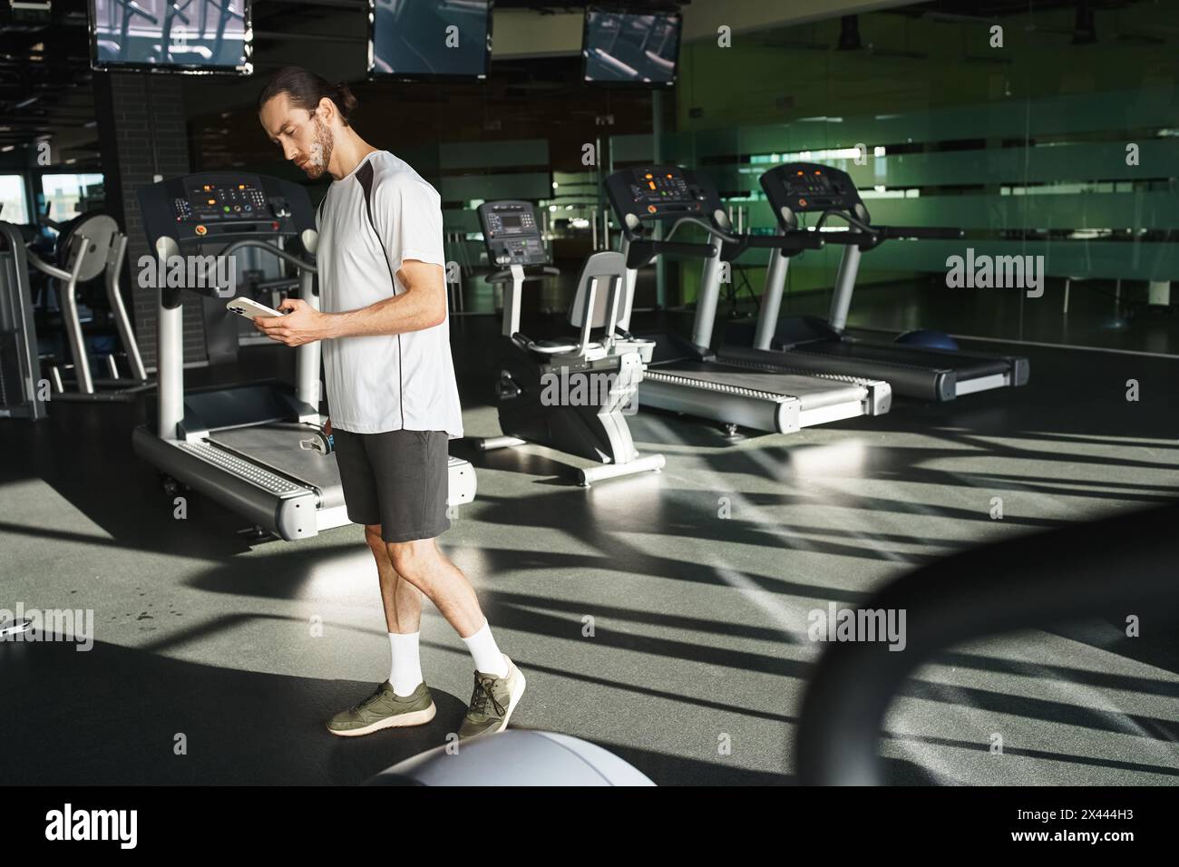 A muscular man in activewear checking his cell phone while taking a break from his workout ...